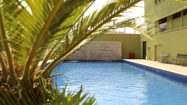 Uma piscina interna com água azul cristalina, cercada por um muro baixo e um muro de textura de pedra ao fundo.