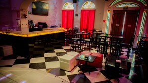 Uma área de bar com piso xadrez, cortinas vermelhas e balcão.