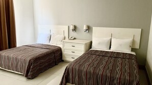 Quarto de hotel com duas camas, mesa de cabeceira, abajur e telefone.