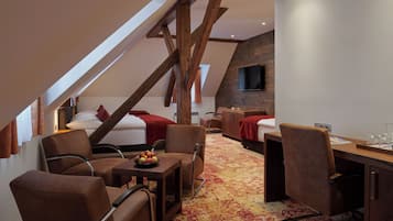 Quarto de hotel moderno com teto inclinado, vigas de madeira, televisão de tela plana, escrivaninha com cadeira e duas camas com roupa de cama vermelha.
