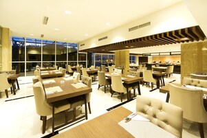 Um amplo hall de hotel com várias áreas de refeição, grandes janelas e design moderno.