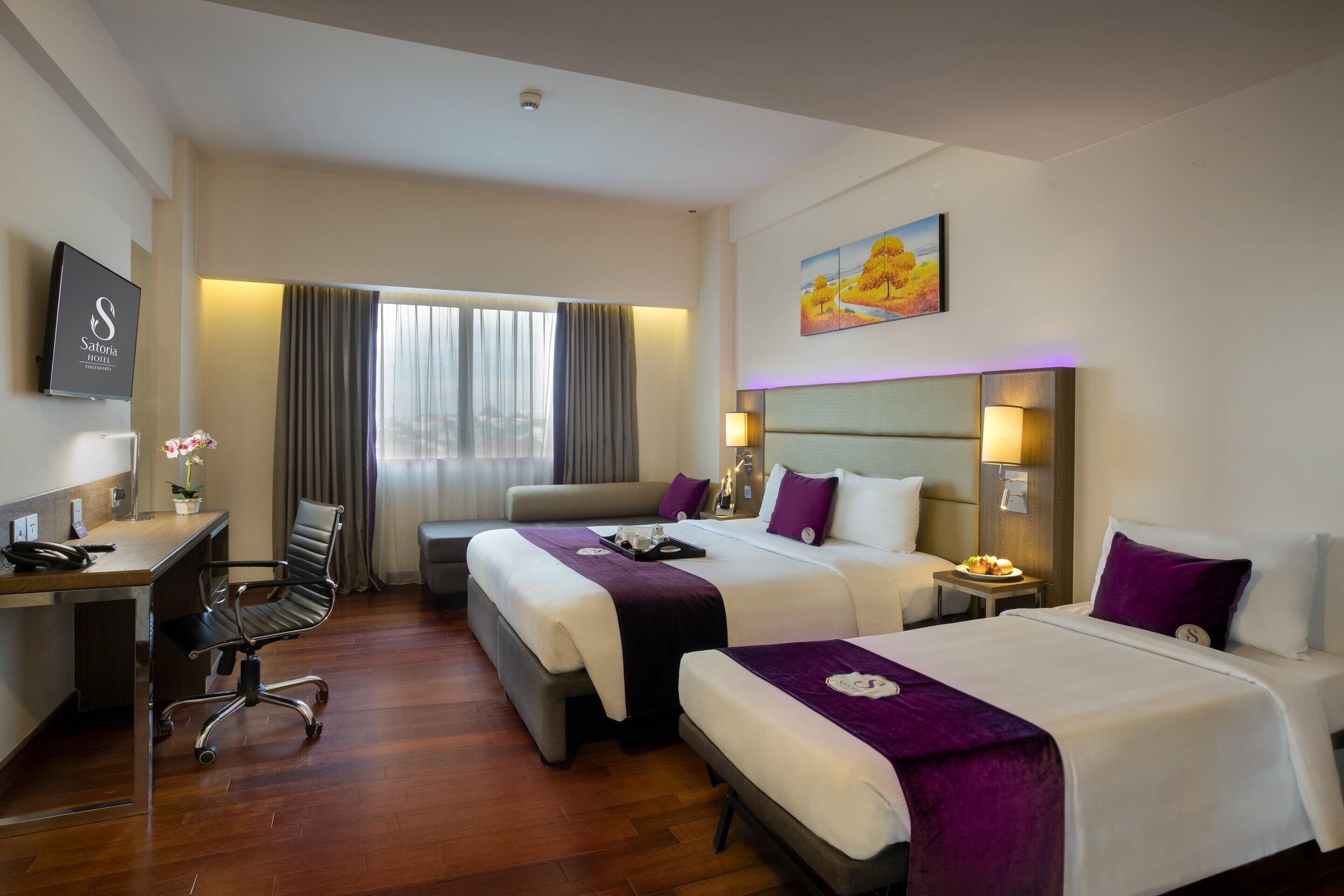 Quarto de hotel com duas camas, uma escrivaninha, uma cadeira, uma mesinha e uma janela com cortinas.