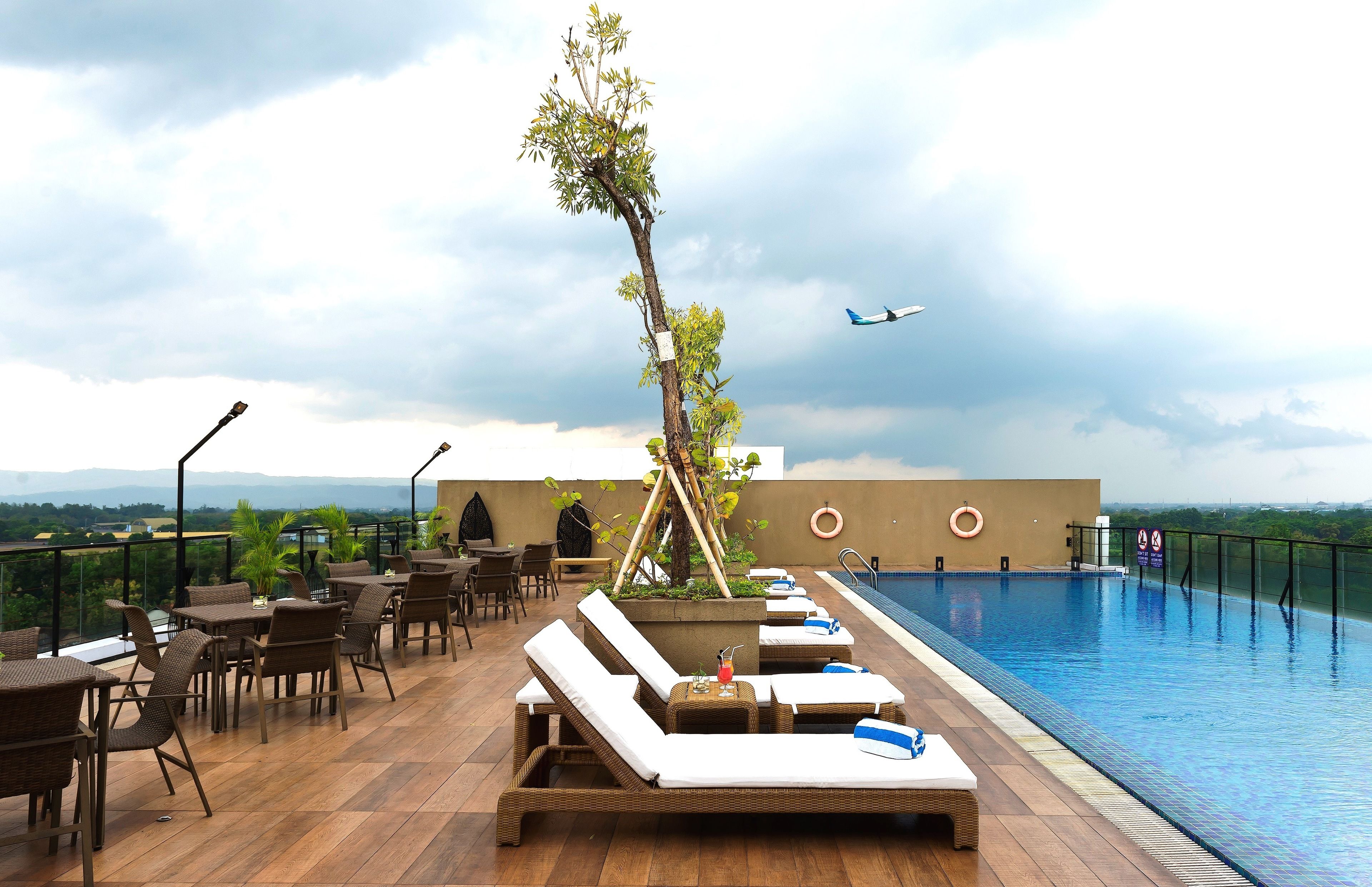 Uma área de piscina no terraço, com espreguiçadeiras, mesas e vista para o céu.