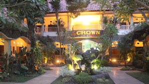 Um hotel com uma placa grande que diz "Crown Hotel", rodeado por vegetação exuberante e um jardim bem cuidado com um elemento central de água.