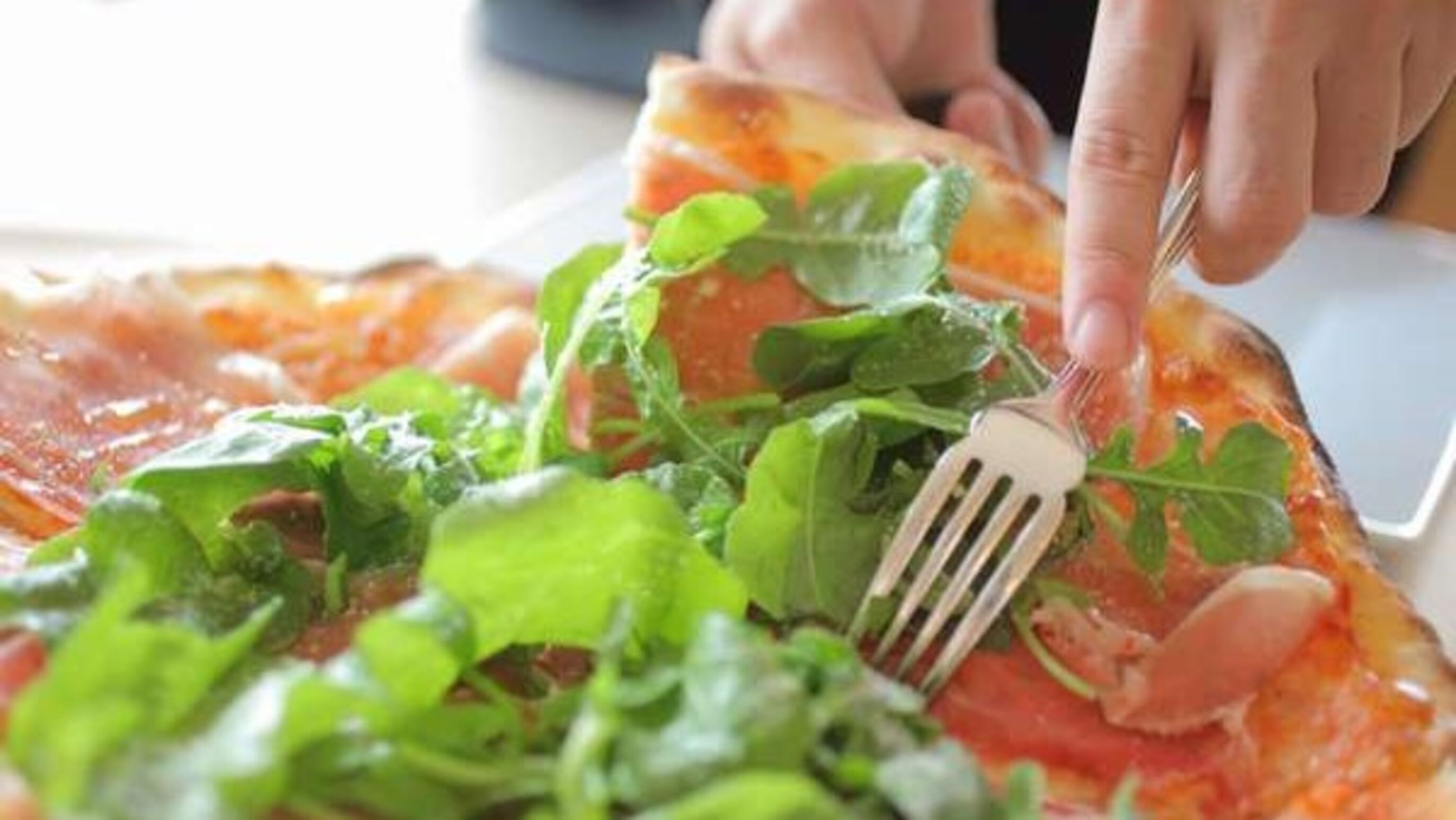 Pizza com folhas verdes e um garfo sobre um prato branco.