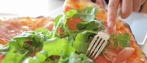 Pizza com folhas verdes e um garfo sobre um prato branco.