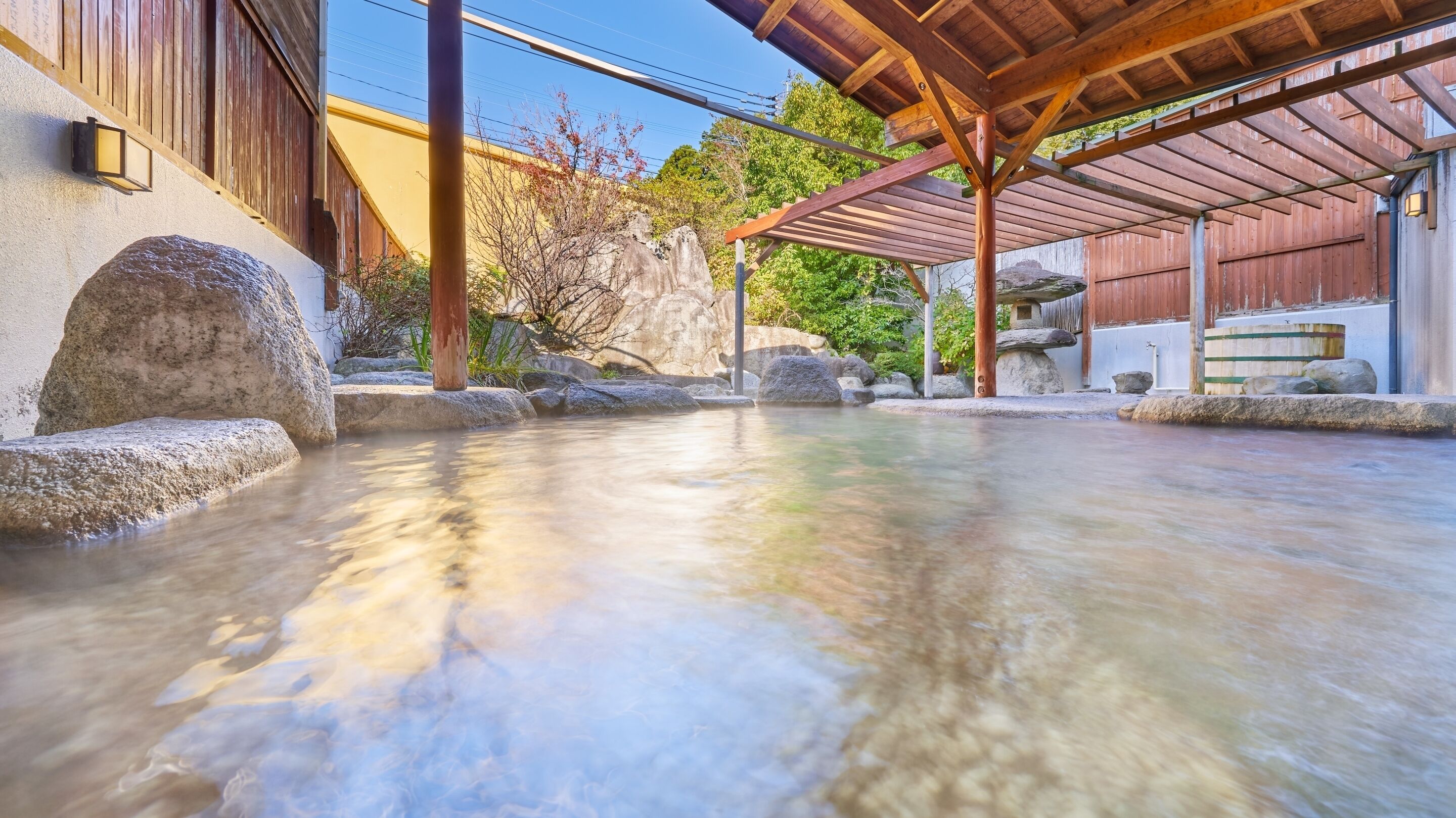 Uma onsen japonesa tradicional com estrutura de madeira, banheira de pedra e paisagem natural.