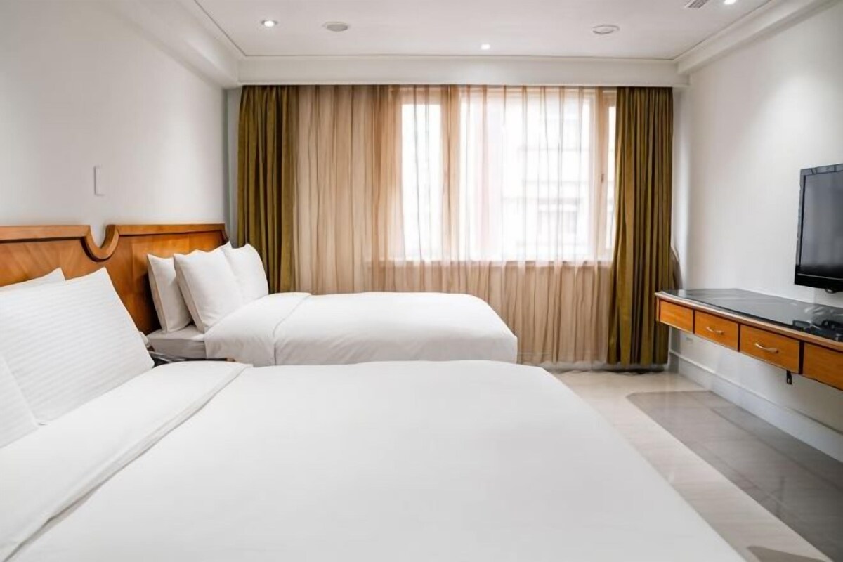 Quarto de hotel com duas camas, televisão e janela com cortinas.