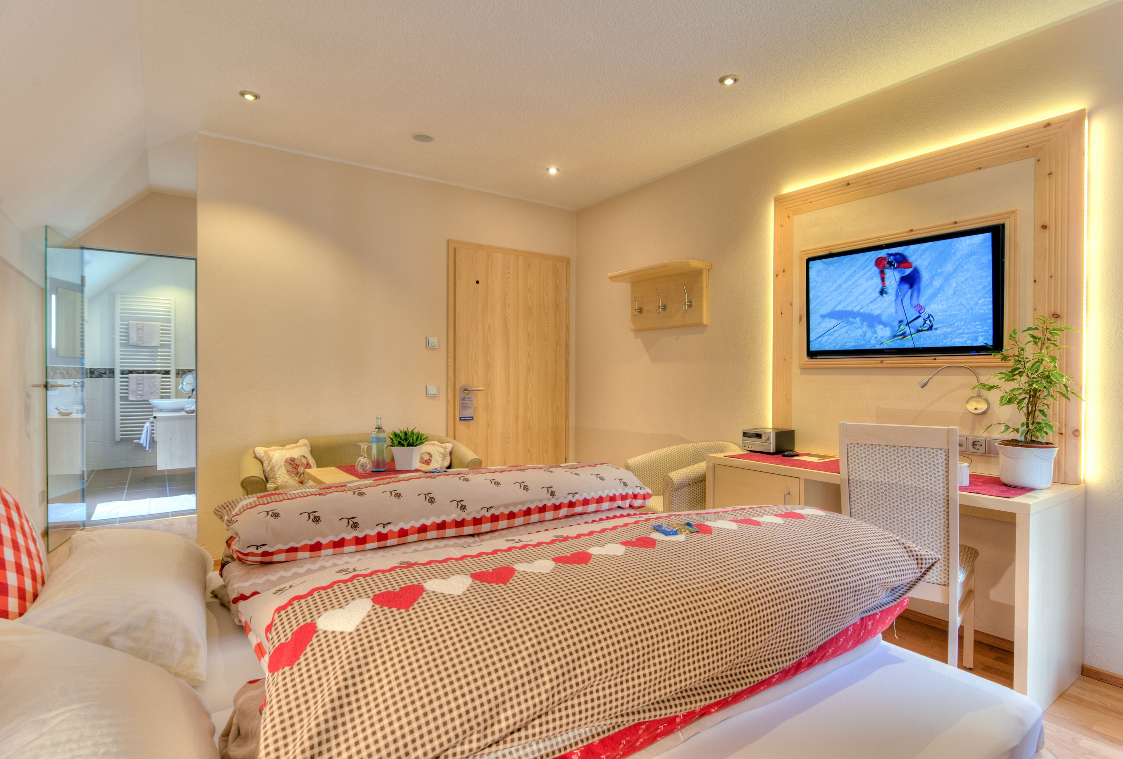 Quarto de hotel moderno com uma cama grande, uma escrivaninha, uma cadeira, uma televisão e um vaso de planta.
