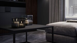Uma sala de estar moderna com esquema de cores escuras, apresentando um sofá, uma mesa com velas e um aplique de parede.
