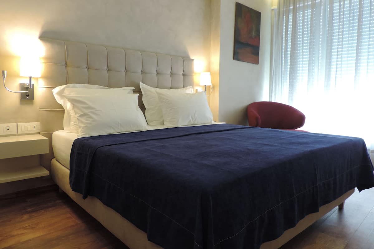 Quarto de hotel com cama, abajures, uma cadeira vermelha e um quadro na parede.