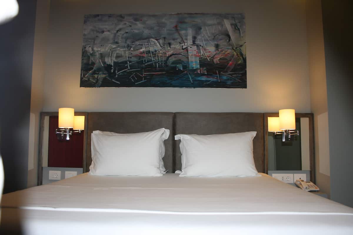 Quarto de hotel com uma cama grande, duas luminárias de cabeceira e um quadro na parede.