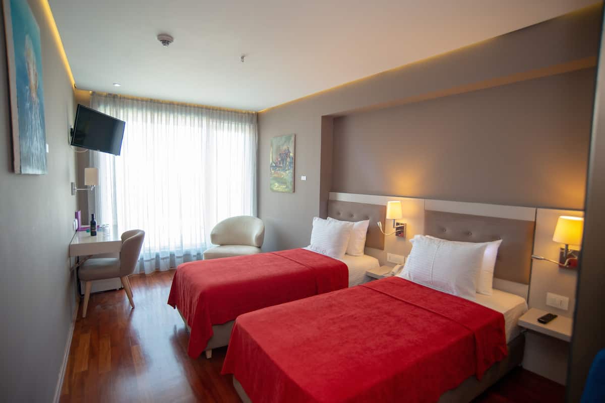 Quarto de hotel com duas camas, uma escrivaninha, uma cadeira, uma televisão e um quadro na parede.