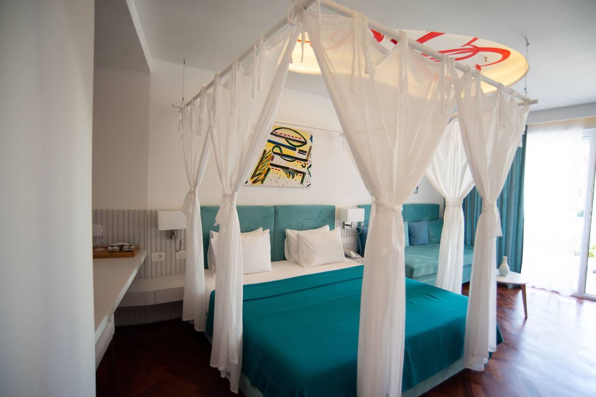 Quarto com cama sob um dossel branco, roupa de cama verde-água e design moderno.