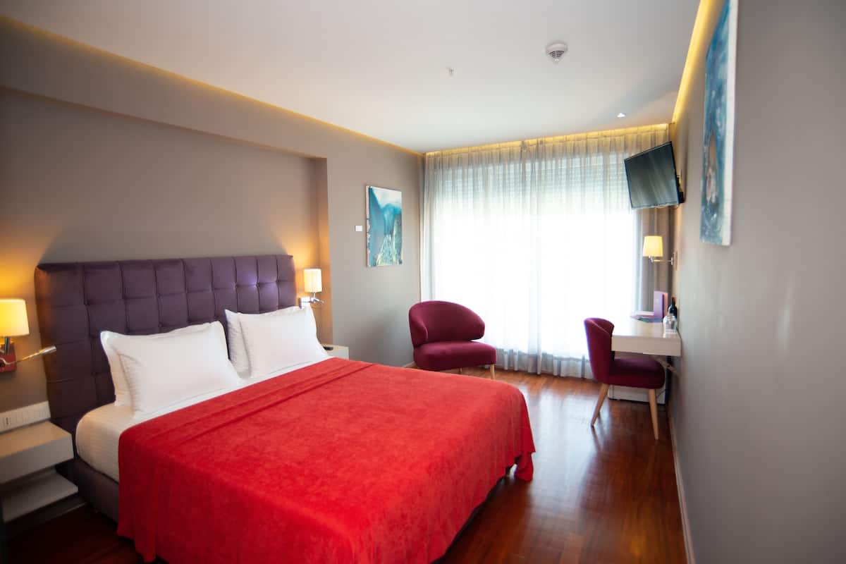 Quarto de hotel com uma cama grande, uma escrivaninha com cadeira, televisão e janela com cortinas.
