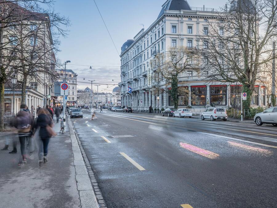 Uma rua com edifícios, carros e pedestres.