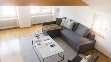 Uma sala de estar moderna com um sofá cinzento, uma mesa de centro e uma luminária.