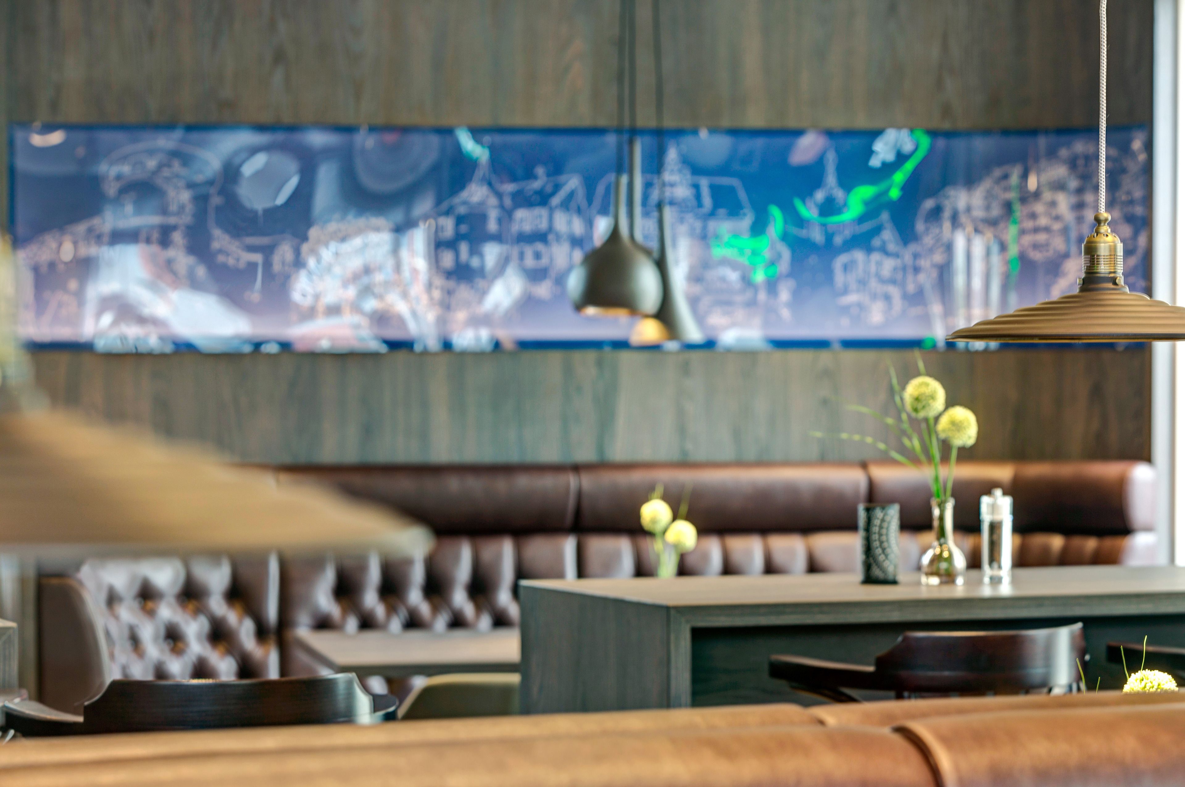 Interior de restaurante com parede longa de painéis de madeira, assentos acolchoados, luminárias pendentes e uma pequena mesa com um vaso de flores.