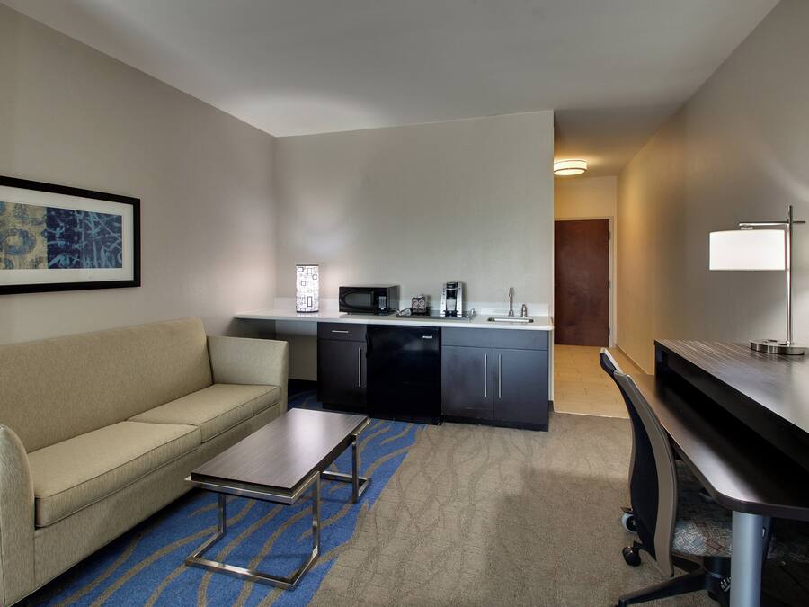 Quarto de hotel com cozinha compacta, sofá, escrivaninha e cadeira.