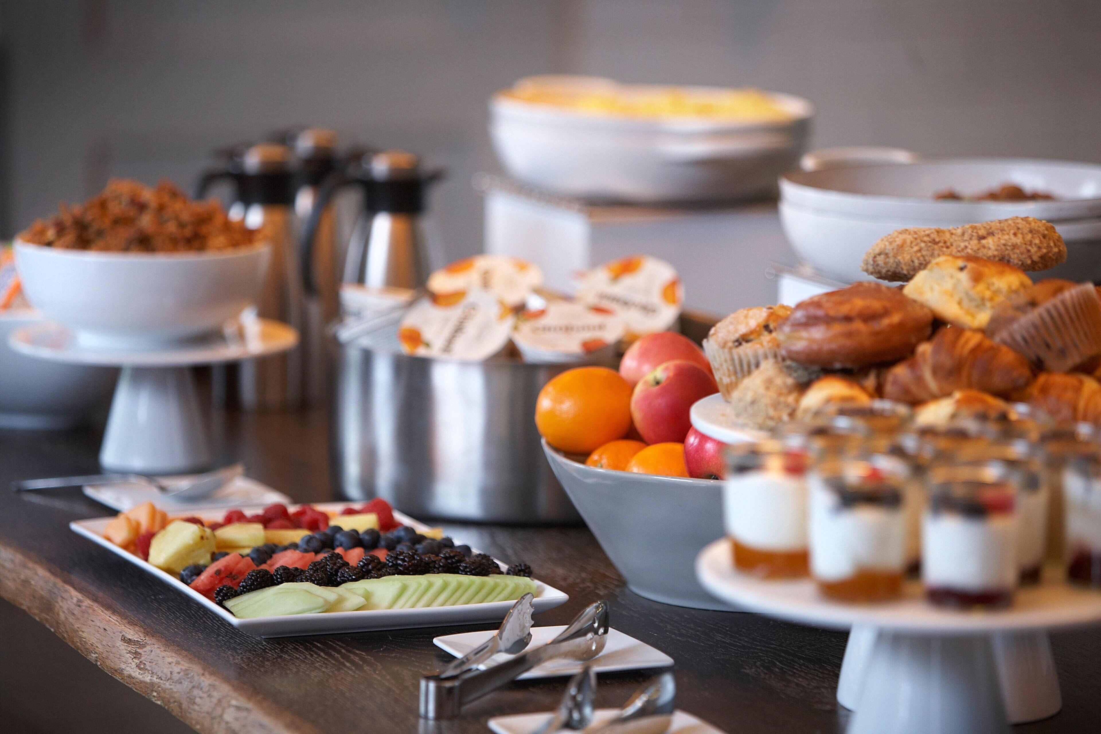 Uma mesa de buffet com diversos alimentos, incluindo frutas, doces e sobremesas.