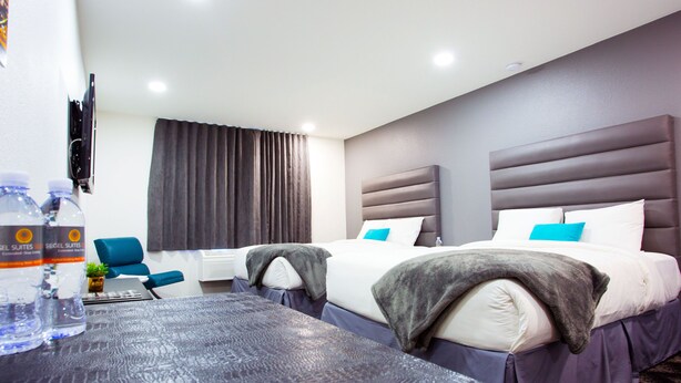 Quarto de hotel com duas camas, uma escrivaninha com cadeira, televisão e janela com cortinas.