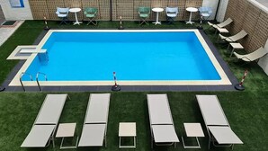 Piscina retangular com interior azul, rodeada por um espaço gramado e cadeiras de descanso brancas.