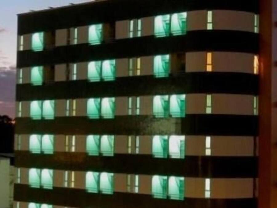 Um edifício com vários andares e inúmeras janelas, algumas delas iluminadas.