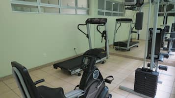 Academia com equipamentos de cardio, pesos e um espelho grande.