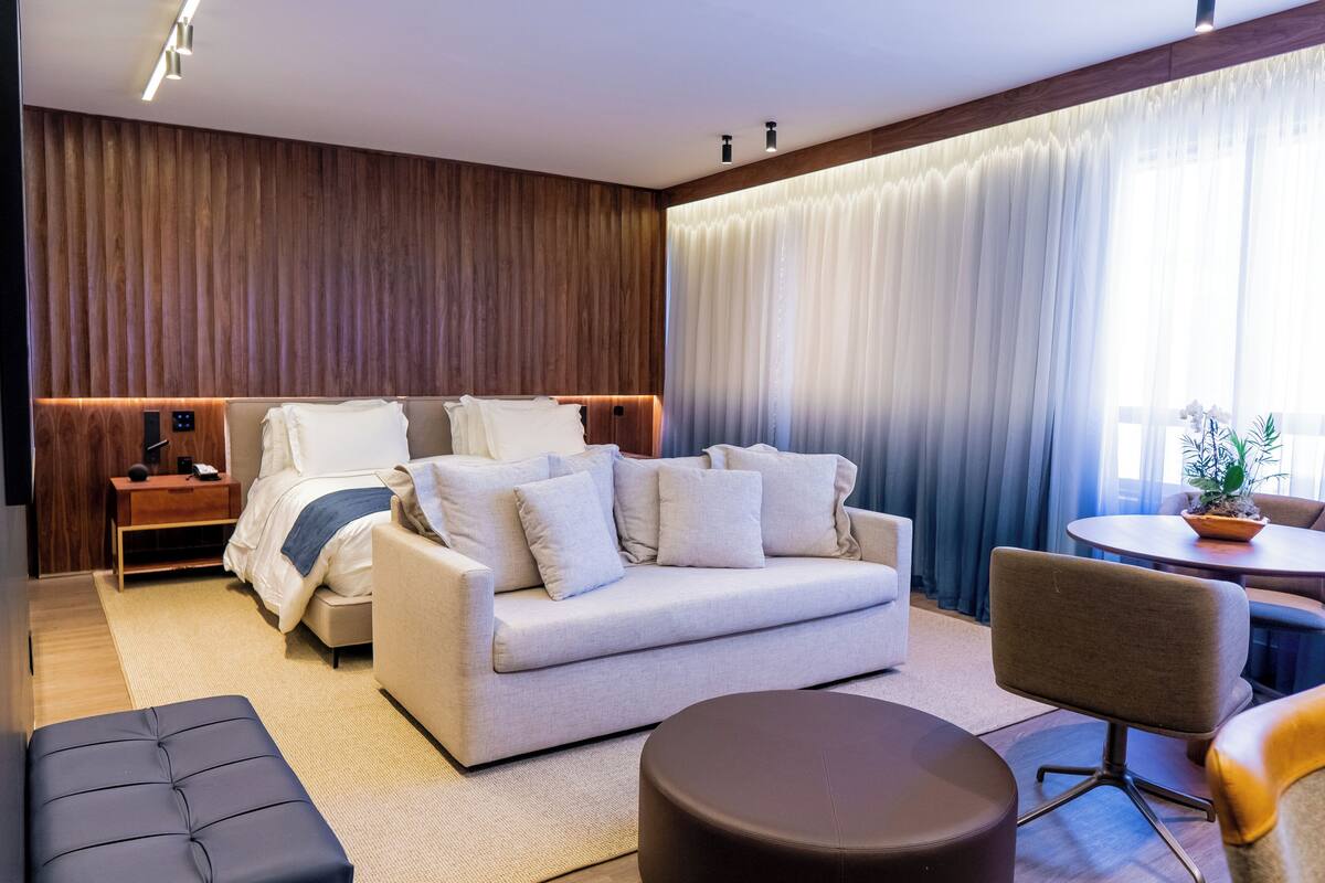 Quarto de hotel moderno com uma cama, um sofá, uma mesa redonda e uma cadeira.