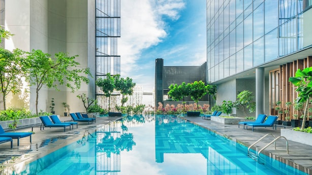 Piscina interior moderna com água azul cristalina, rodeada por espreguiçadeiras e plantas em vasos.