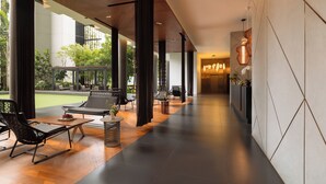 Um hall de hotel moderno com um corredor longo, áreas de estar e grandes janelas com vista para um jardim.