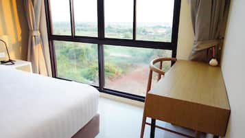 Quarto de hotel com uma cama, uma mesa e uma grande janela com vista para uma paisagem verde.