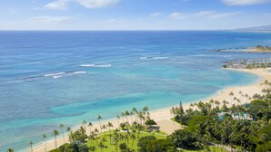 Vista costeira com águas azul-claras, uma praia arenosa e vegetação exuberante.