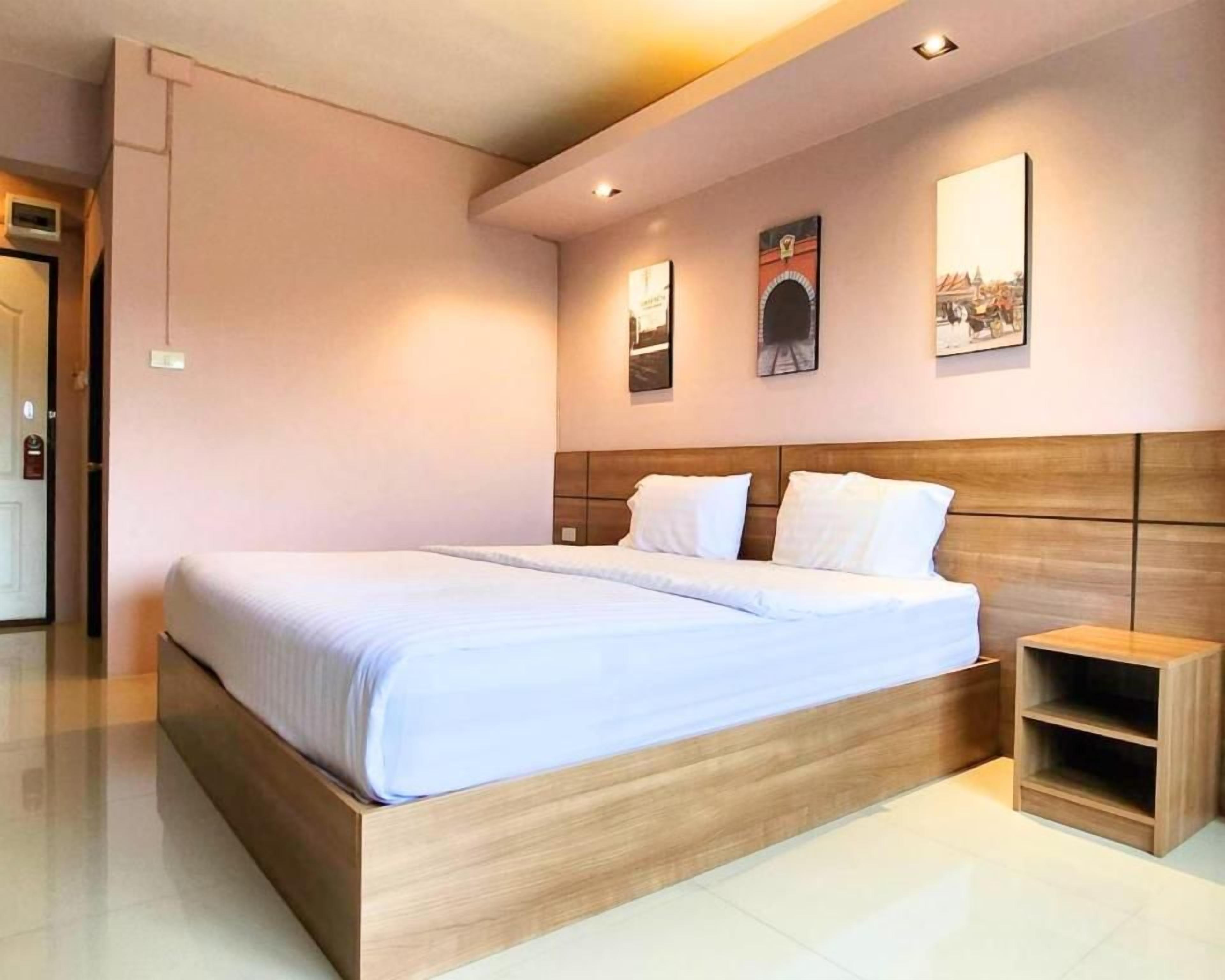 Quarto de hotel moderno com estrutura de cama de madeira, roupa de cama branca e uma pequena mesa de cabeceira de madeira.