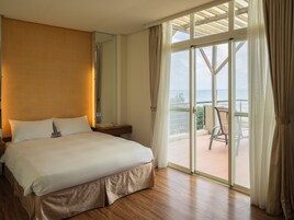 Quarto de hotel com uma cama grande, cabeceira de madeira, mesa de cabeceira, espelho e varanda com uma cadeira.