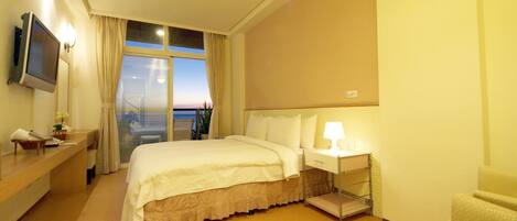 Quarto de hotel com cama, mesa de cabeceira, cadeira e televisão na parede.