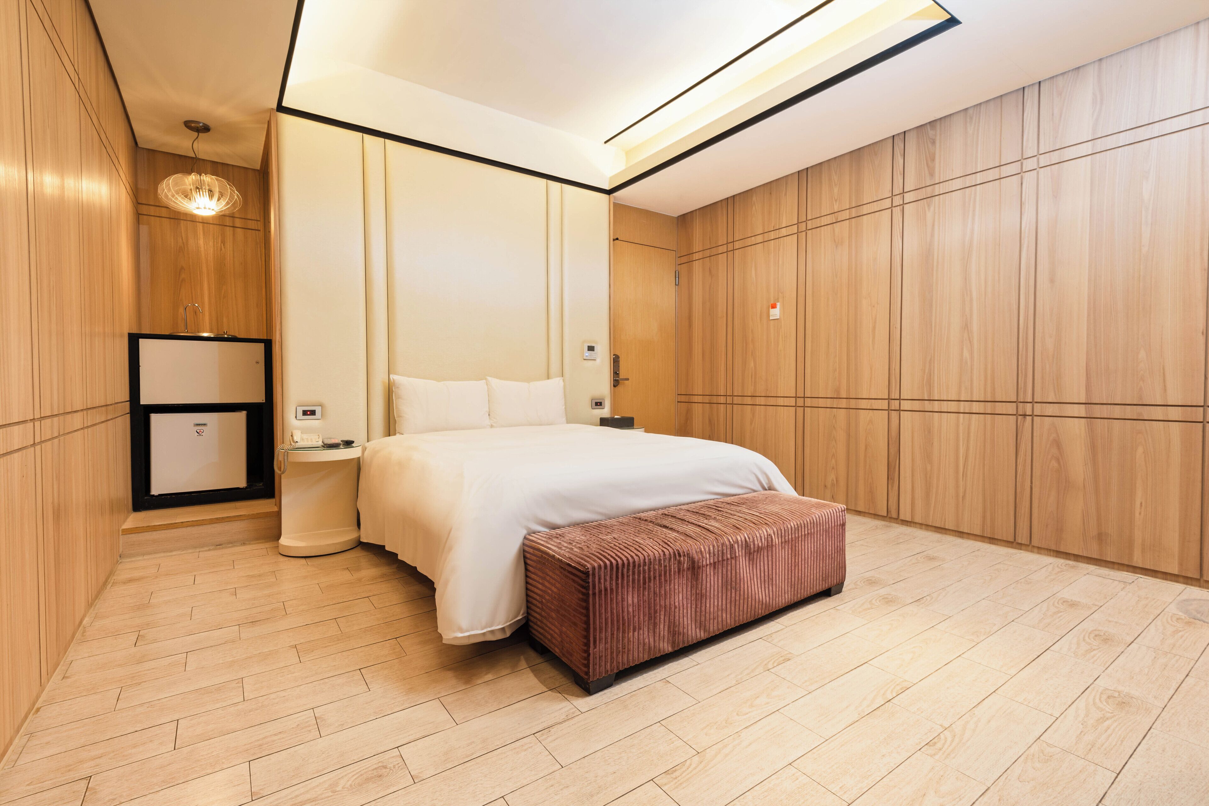 Quarto moderno com cama grande, mesa de cabeceira, criado-mudo e roupeiro embutido, além de um pequeno armário.