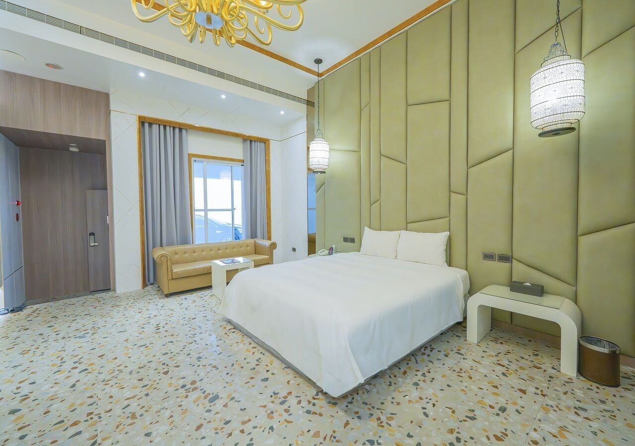 Quarto de hotel moderno com uma cama grande, um sofá, uma mesinha e um lustre decorativo.