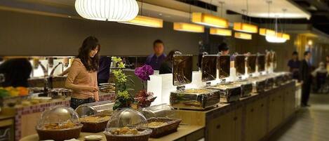 Disposição de buffet com diversos alimentos e uma pessoa servindo.