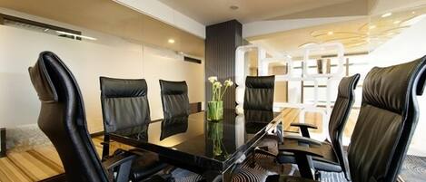 Uma sala de conferências com mesa de vidro, cadeiras de couro preto e um vaso com flores brancas.