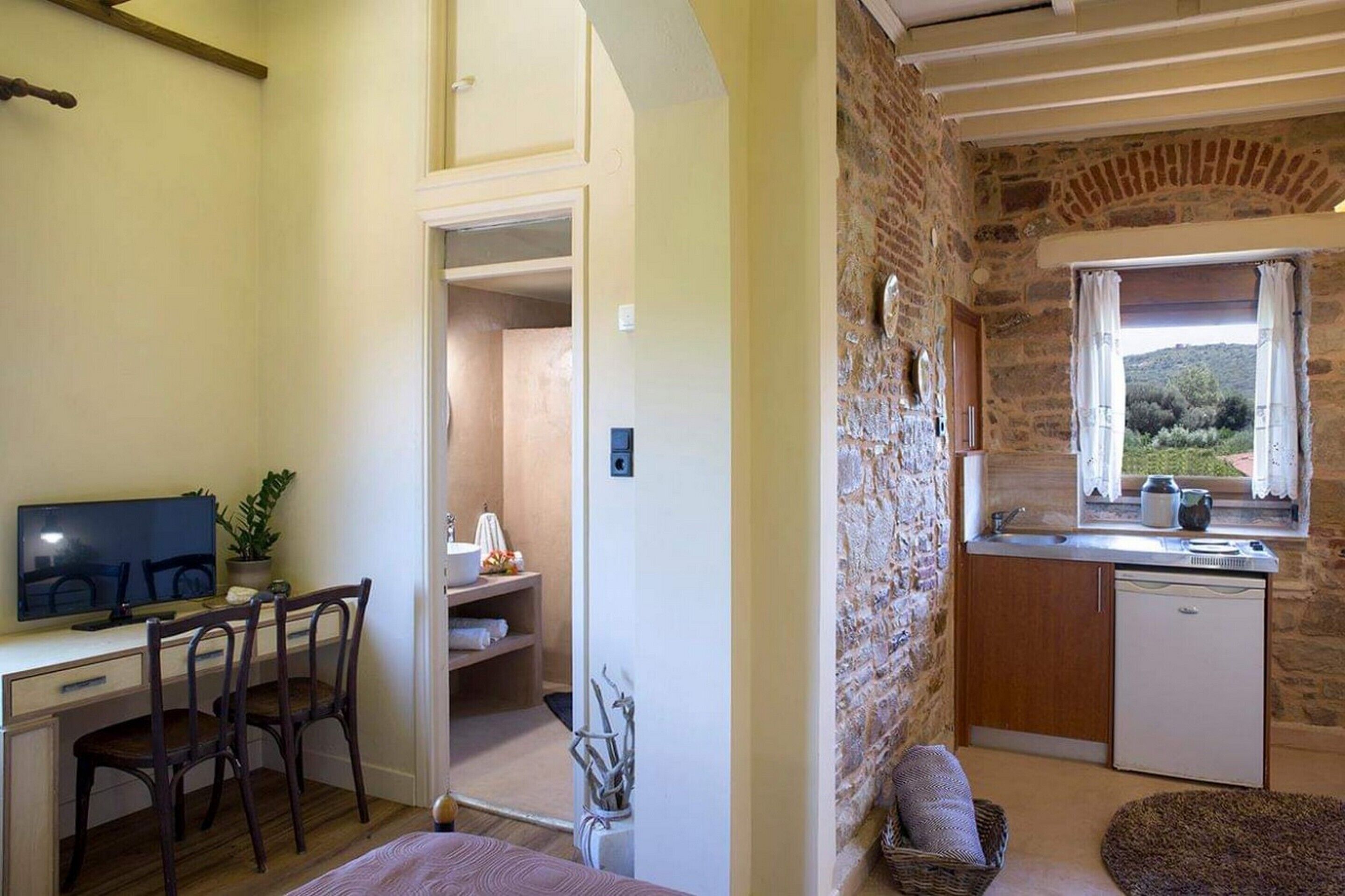 Quarto compacto com escrivaninha, cadeira e cama. Possui uma pequena cozinha compacta com pia e janela com vista para o exterior.