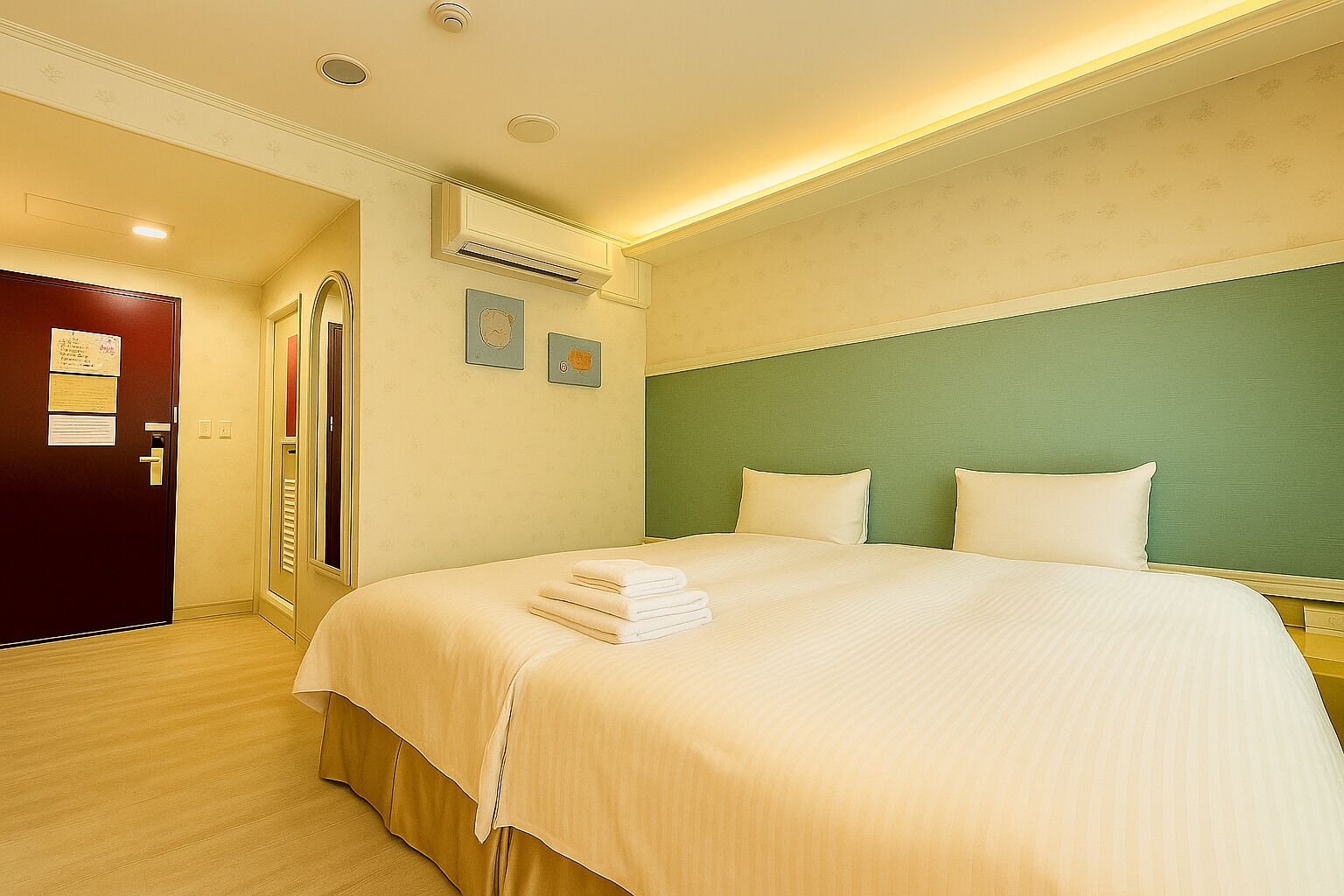 Quarto de hotel com uma cama grande, duas almofadas, cabeceira, porta e ar condicionado fixado na parede.