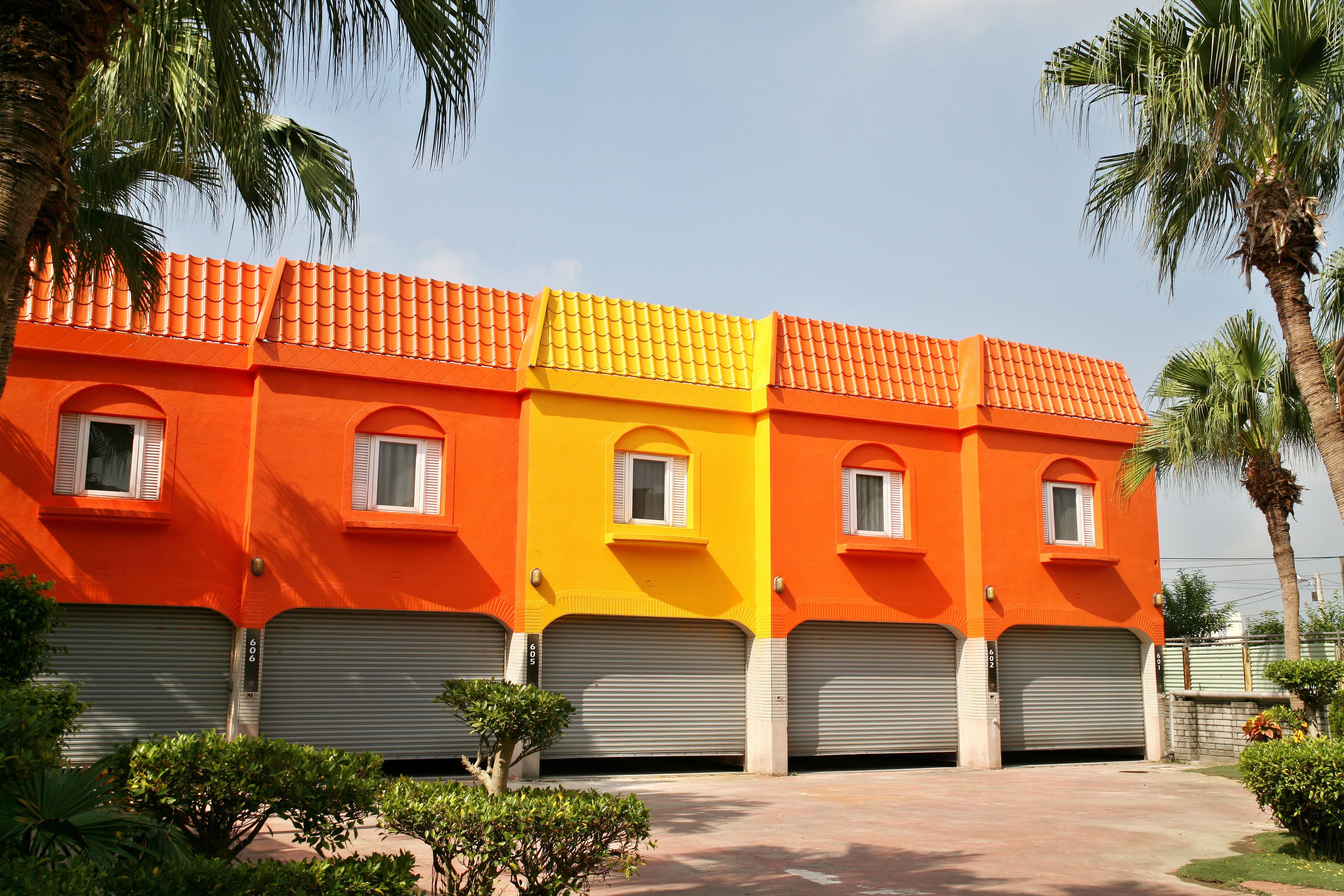 Um edifício com várias fachadas laranja e amarelo, grandes portões de garagem e um caminho de acesso pavimentado.