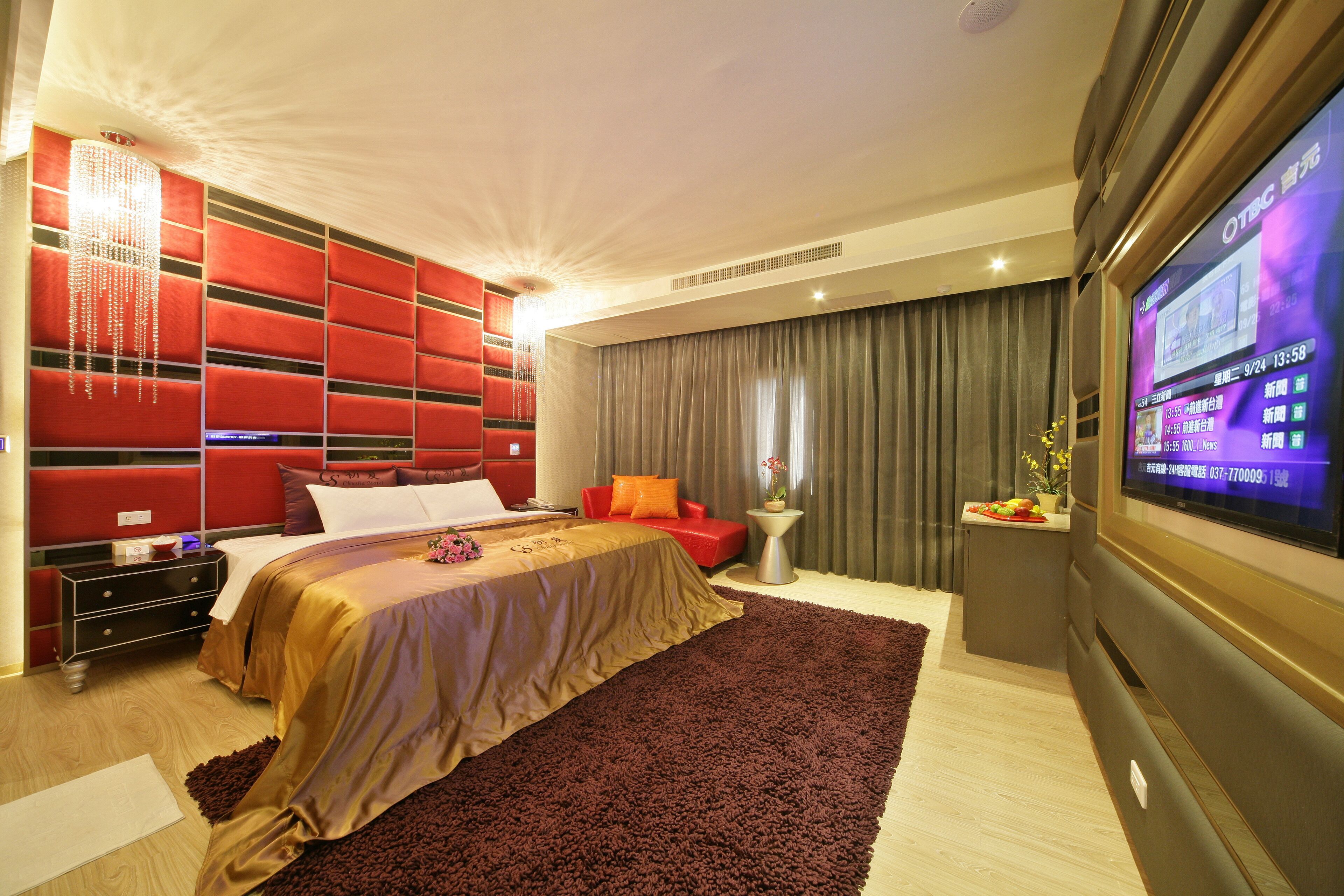Quarto de hotel moderno com uma cama grande, um sofá vermelho, uma televisão e uma pequena mesa com uma planta.