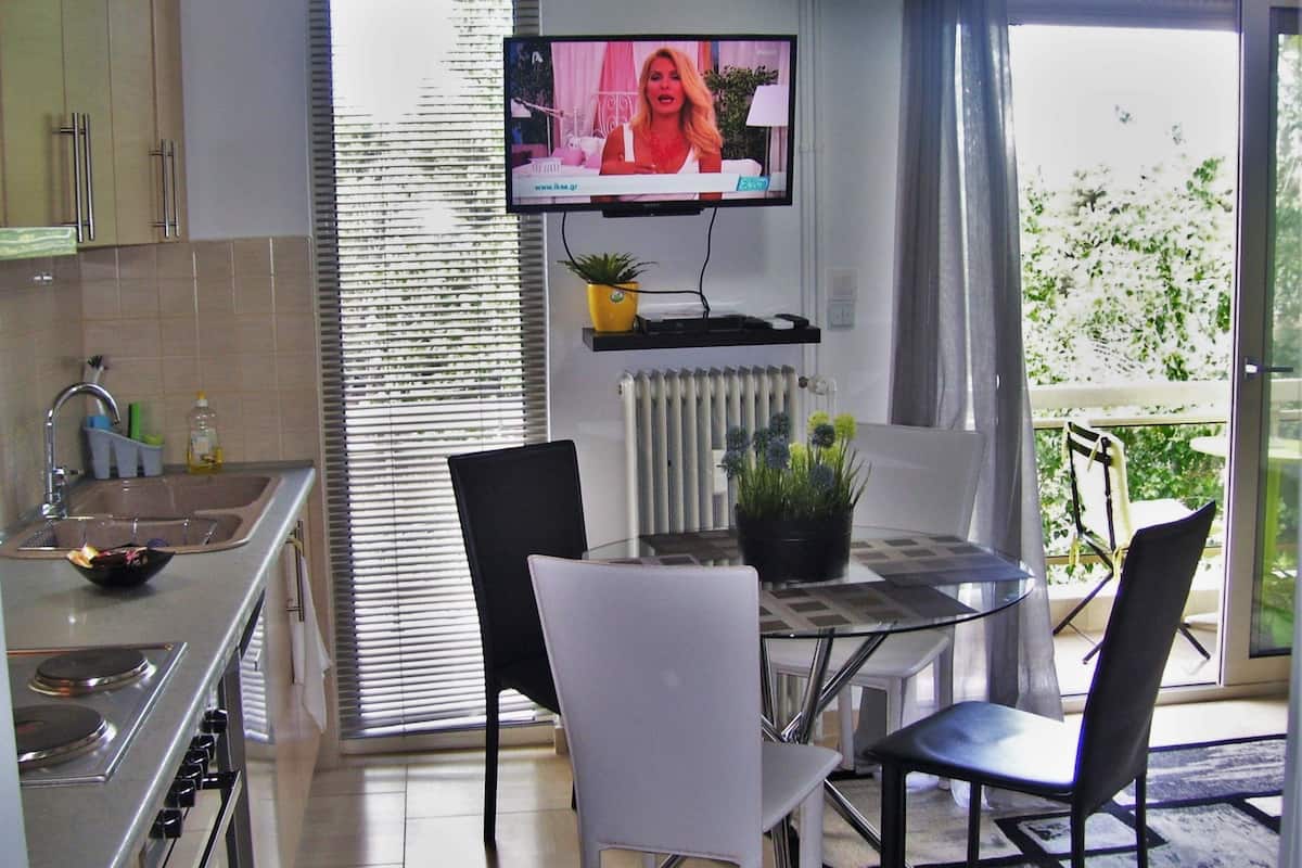Cozinha moderna com fogão embutido, pia e área de refeições com mesa e cadeiras. Há uma TV na parede exibindo um programa.