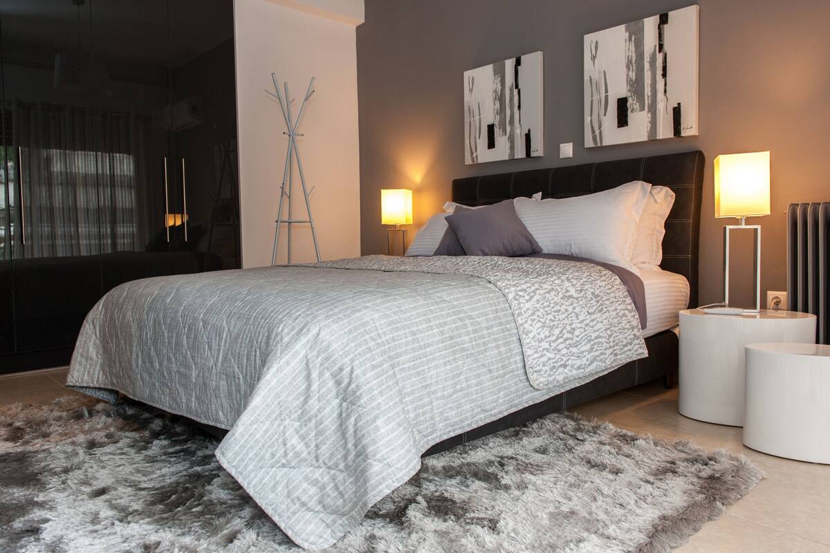 Quarto moderno com uma cama grande, duas luminárias de cabeceira, um tapete macio e arte abstrata na parede.