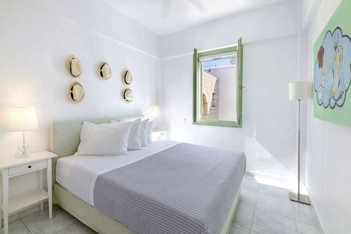 Quarto com cama, mesas de cabeceira, abajur, espelho e obras de arte nas paredes.