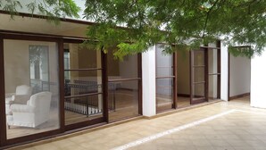 Corredor com grandes portas de vidro deslizantes que dão para uma varanda com uma cadeira branca.