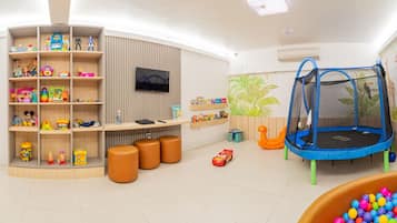 Uma sala de jogos infantil com televisão, prateleiras cheias de brinquedos, um trampolim e uma piscina de bolinhas.