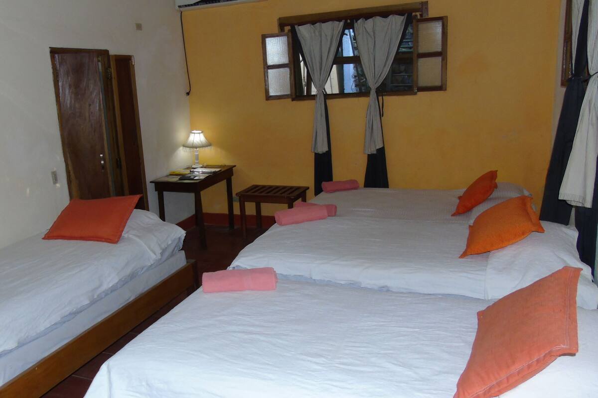Quarto de hotel com duas camas de solteiro, uma mesa pequena com abajur e uma janela com cortinas.